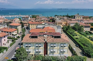 Um hotel com um pátio central, rodeado por edifícios com telhados de cerâmica vermelha, e vista para o mar e para a marina ao fundo.