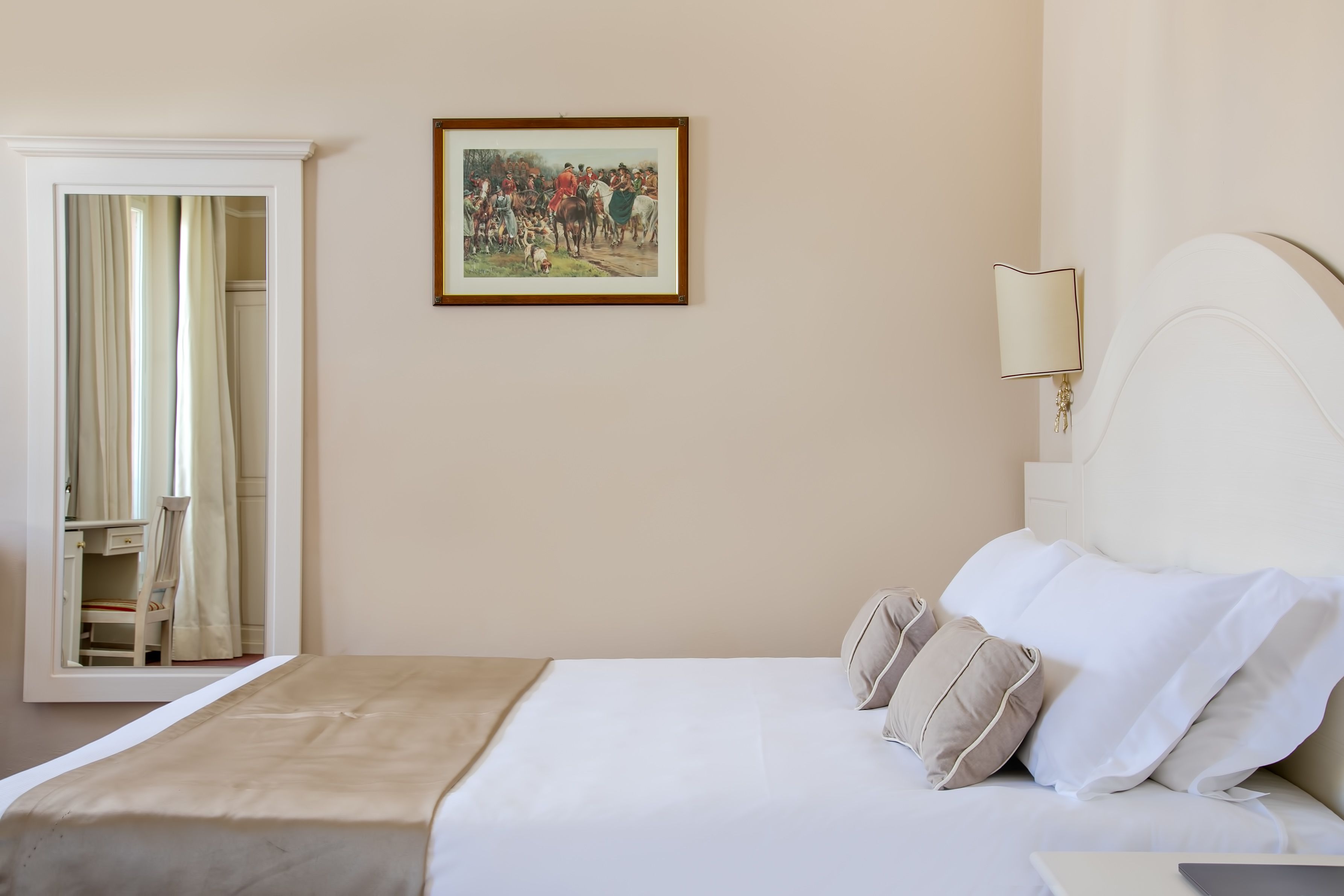 Quarto de hotel com uma cama, um quadro na parede, uma escrivaninha com cadeira e uma luminária.