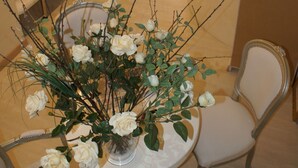 Um saguão de hotel com uma mesa de recepção, um sofá branco, um vaso com flores brancas e uma cadeira.