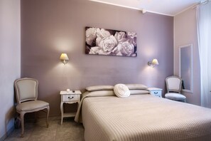 Quarto com cama, duas cadeiras, mesa de cabeceira e luminária na parede.