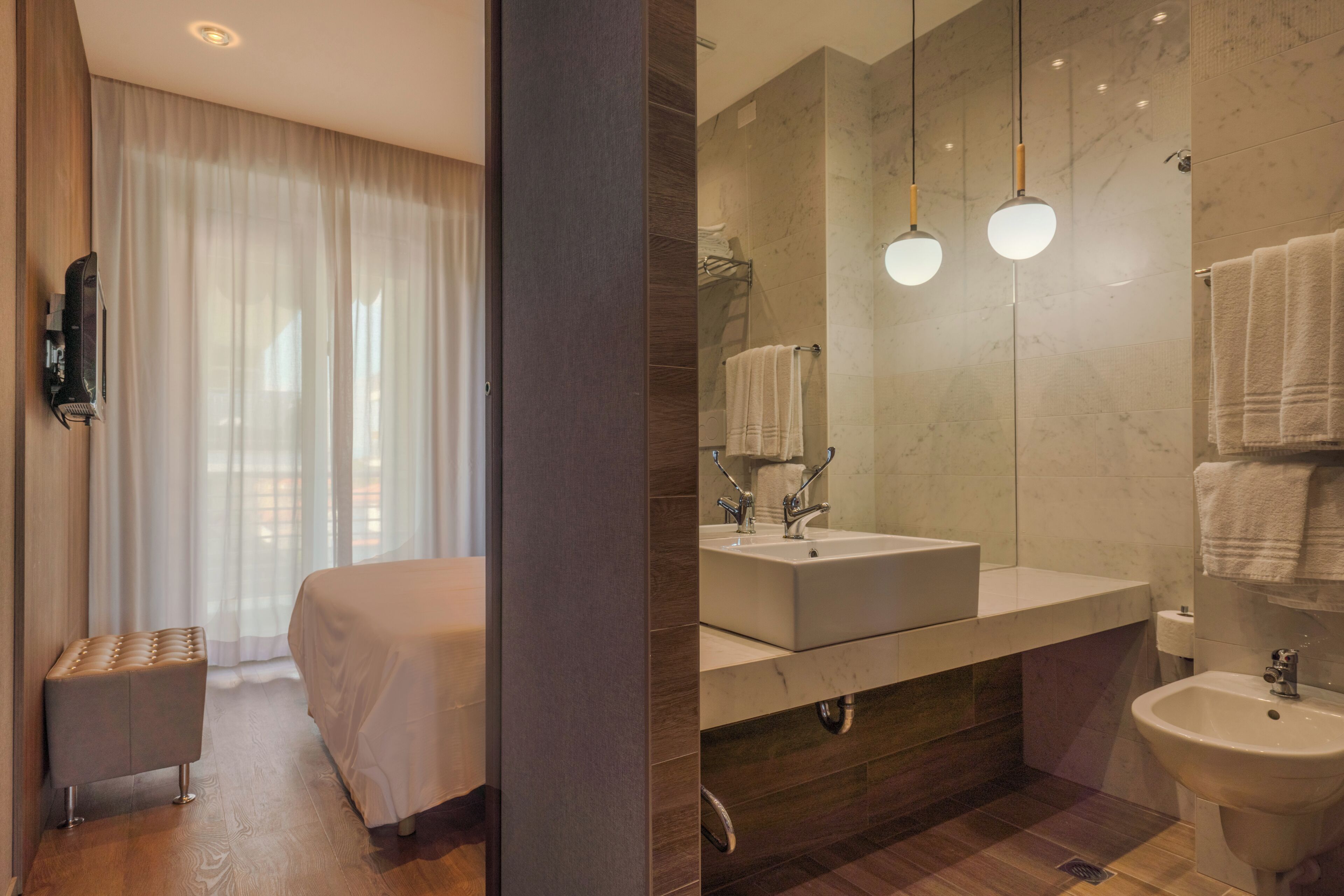 Quarto de hotel com cama, área de estar, espelho grande, pia e bidê.