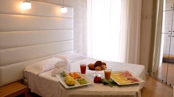 Cama bem arrumada com bandeja de café da manhã contendo frutas, doces e bebidas.