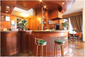 Uma área de bar com balcões de madeira, banquetas estofadas verdes e um aparador de vinhos.