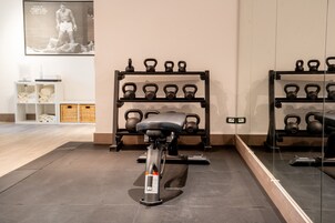 Uma academia com uma bicicleta ergométrica, halteres e um pôster na parede.