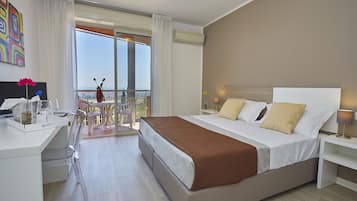 Quarto de hotel moderno com uma cama grande, uma mesa de trabalho e varanda com vista para a cidade.