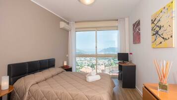 Quarto de hotel com uma cama grande, uma escrivaninha com computador, janela com vista para a cidade e obras de arte na parede.