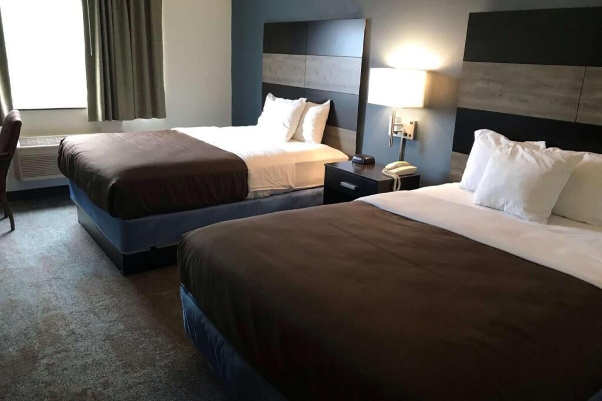 Quarto de hotel com duas camas, uma mesa de cabeceira com abajur e uma janela com cortinas.