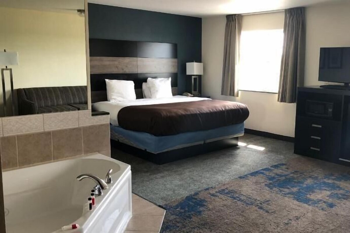 Quarto de hotel com cama, secretária, televisão, banheiro com banheira e janela com cortinas.