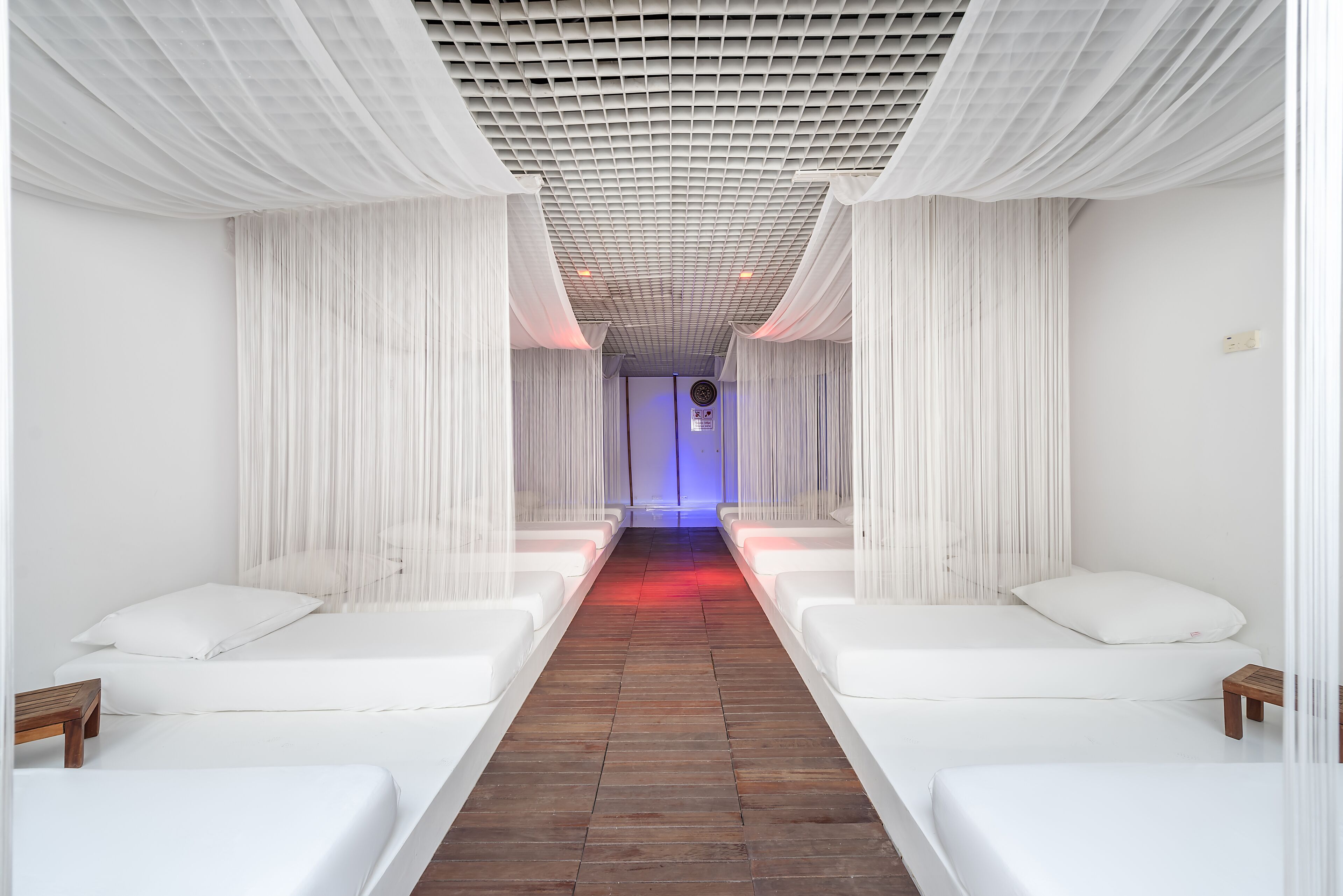 Um quarto de spa com duas camas brancas, piso de madeira e teto com padrão quadriculado.