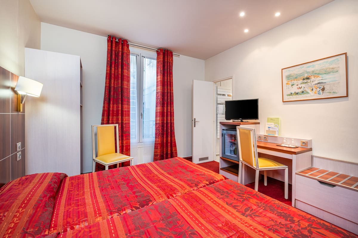Quarto de hotel com cama, escrivaninha, cadeira, televisão e um quadro na parede.