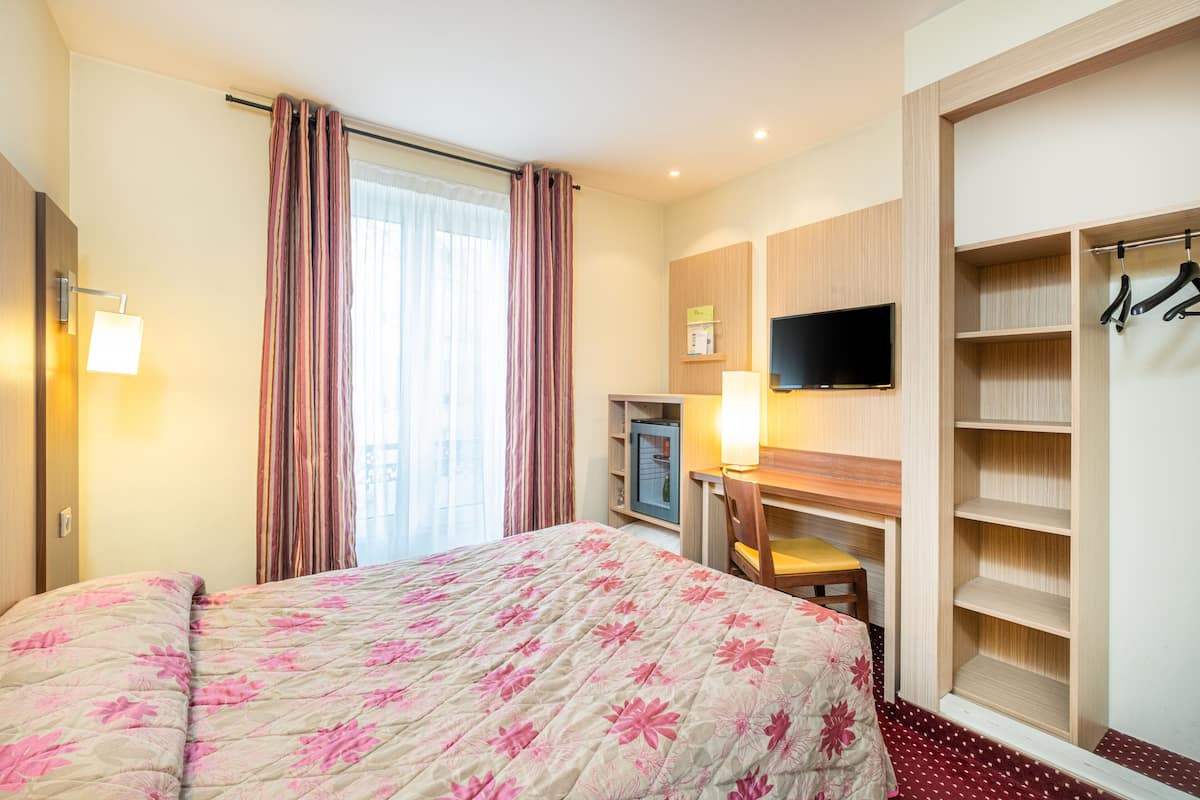 Quarto de hotel com cama, escrivaninha, televisão e armário.