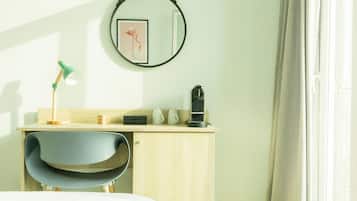 Quarto de hotel com cama, escrivaninha com cadeira, luminária, quadro emoldurado, aquecedor e janela com cortinas.