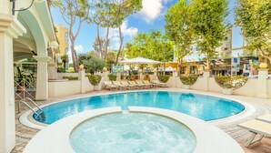 Piscina com espreguiçadeiras, ofurô e área coberta com guarda-sóis.