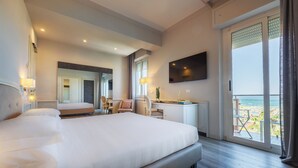 Quarto de hotel com uma cama grande, uma mesa, uma cadeira, uma televisão e varanda com vista para a praia.