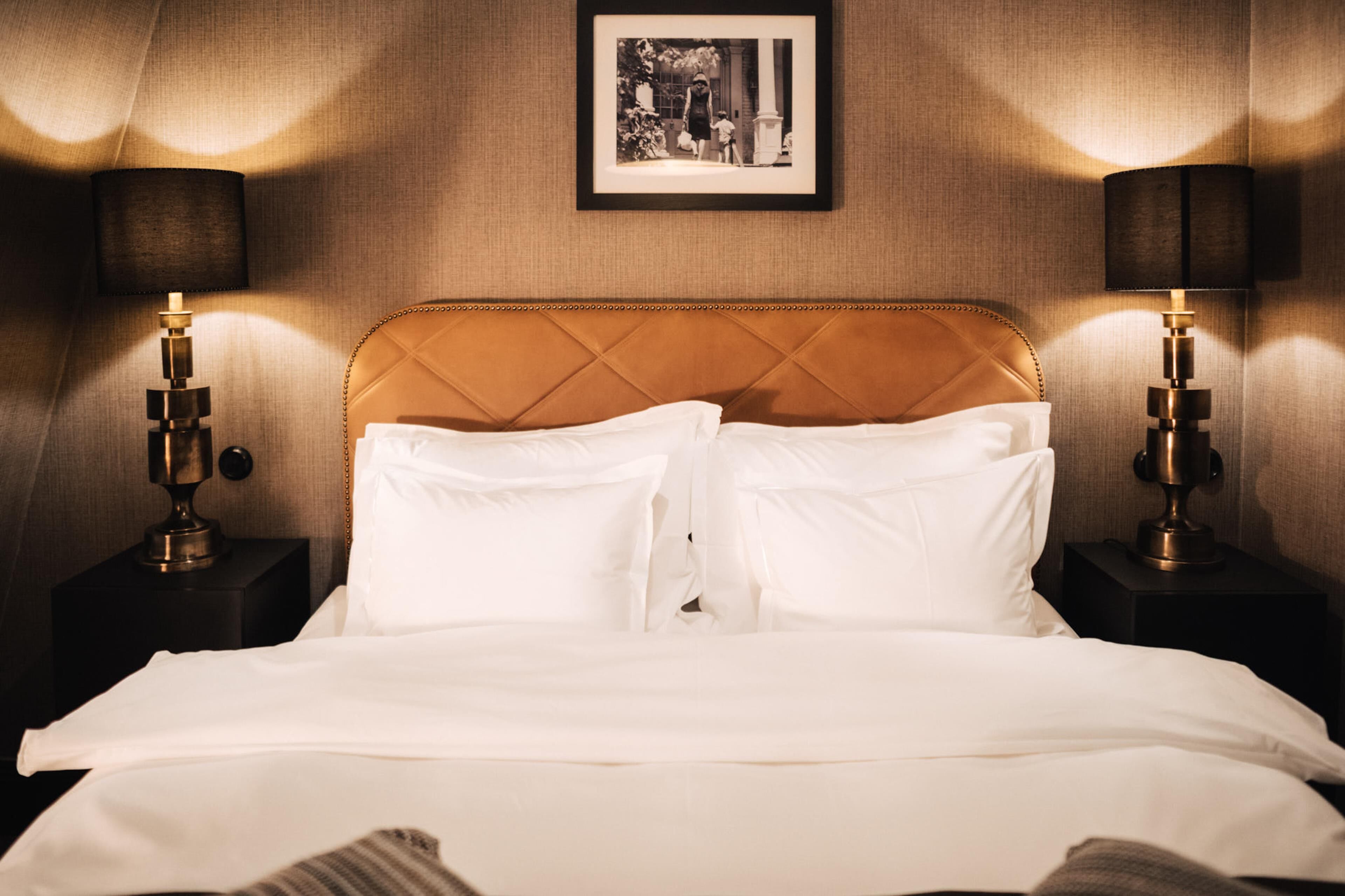Quarto de hotel com uma cama, duas mesas de cabeceira e duas luminárias fixadas na parede.