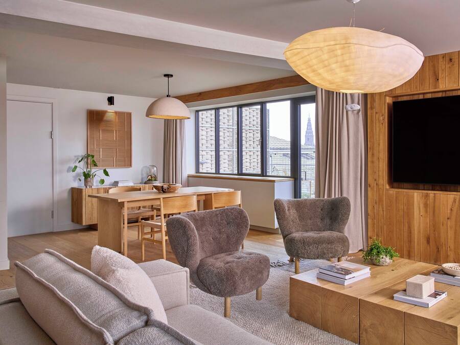 Uma sala de estar moderna com sofá, poltronas, mesa de centro com livros, televisão e um espaço de jantar com mesa e cadeiras de madeira.