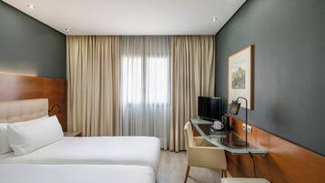 Quarto de hotel com duas camas, uma mesa de trabalho, televisão de tela plana, cafeteira e um quadro na parede.