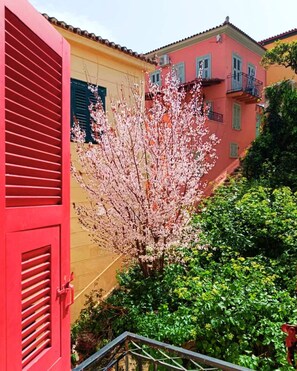 Um edifício com uma porta vermelha e uma árvore florida em tons de rosa à frente.