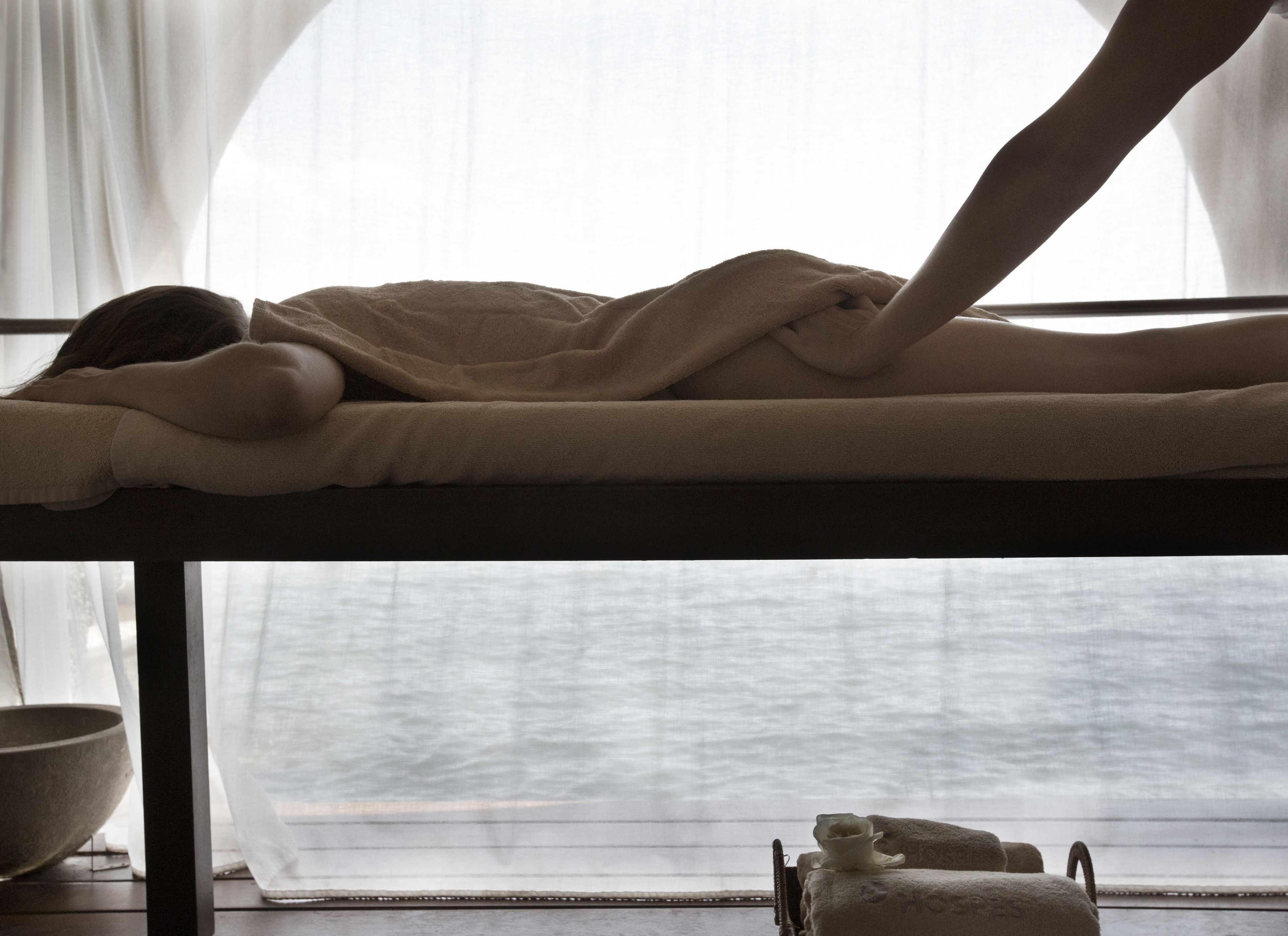Uma pessoa recebendo massagem em uma cama com vista para a janela.