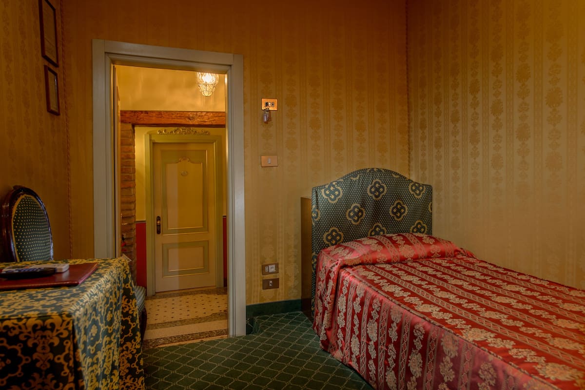 Quarto de hotel pequeno com uma cama de solteiro, uma cadeira e uma mesa.
