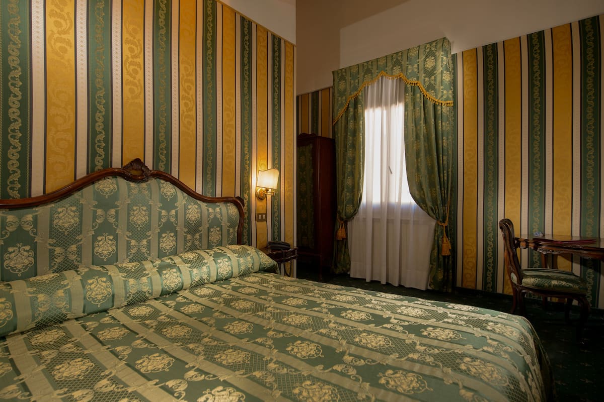 Quarto com uma cama grande, mesa de cabeceira de madeira, escrivaninha e cadeira.