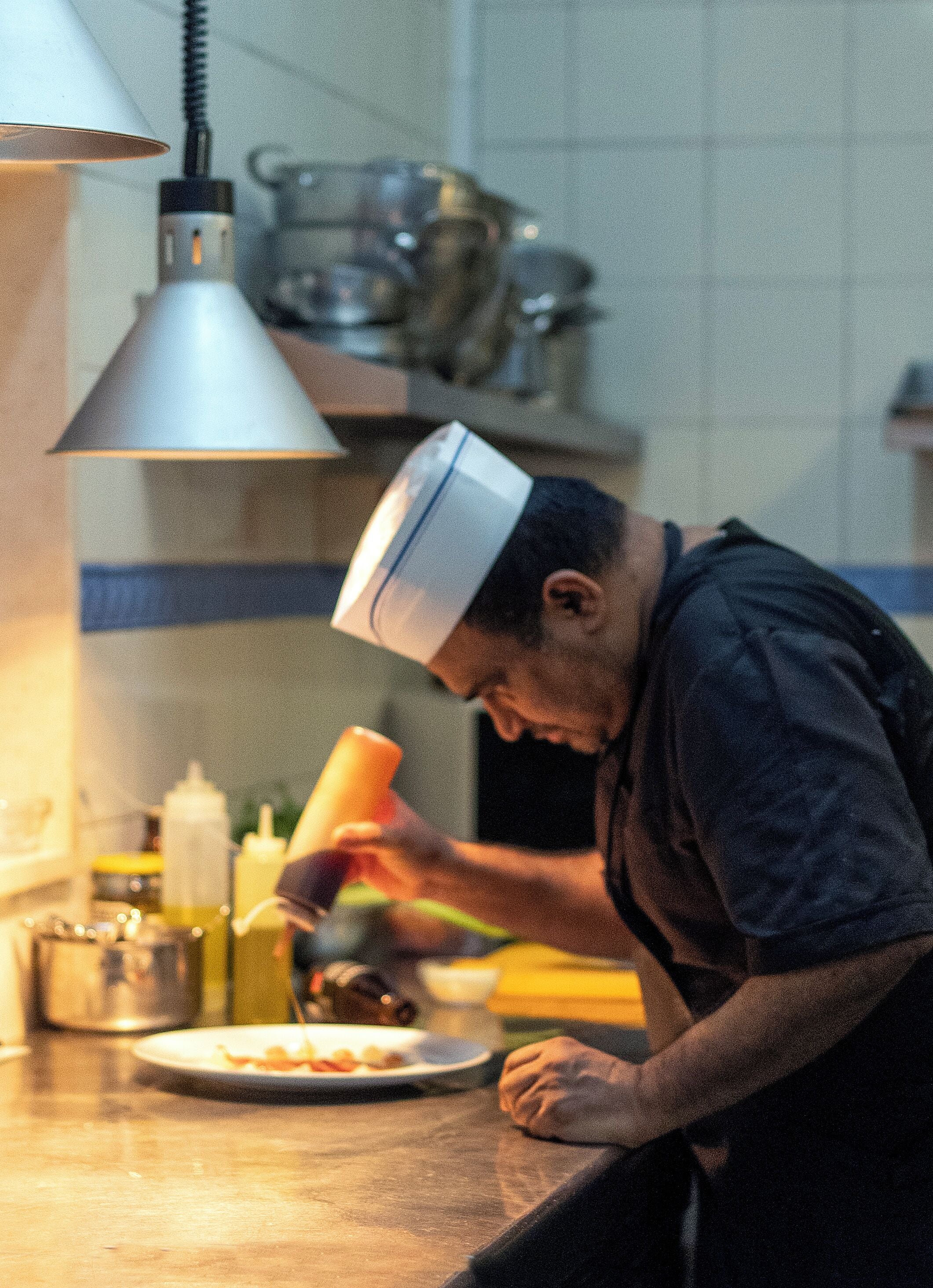 Um cozinheiro em cozinha com uma lâmpada de metal, um prato de comida e utensílios de cozinha.