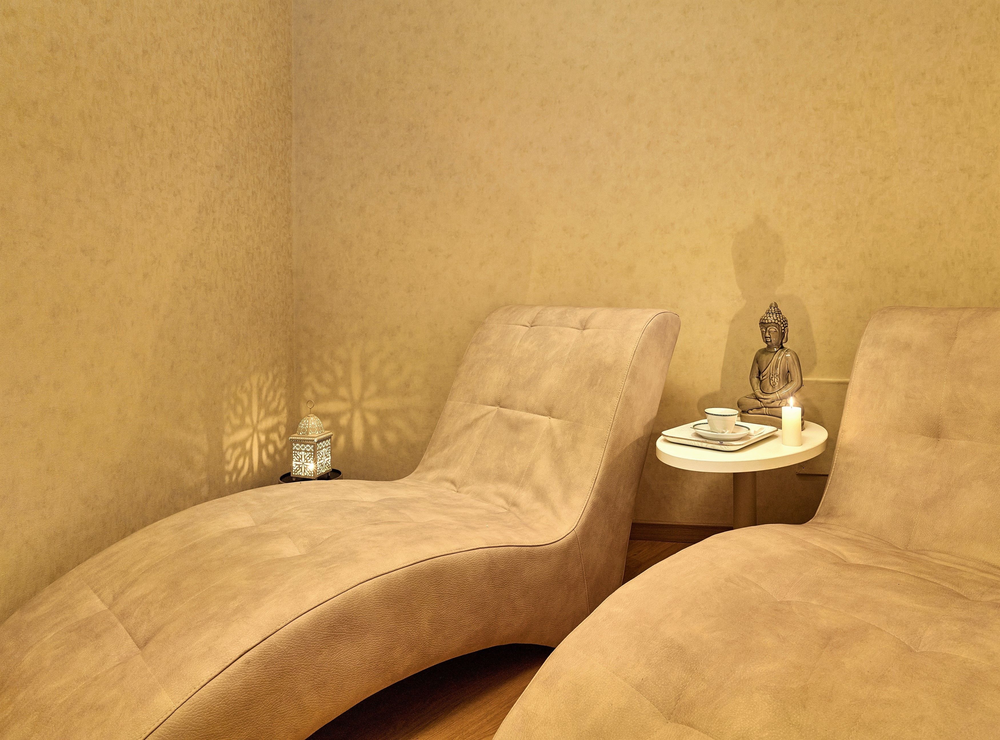 Um quarto com duas poltronas acolchoadas, uma mesa pequena com uma estátua e uma vela, e um candeeiro decorativo.