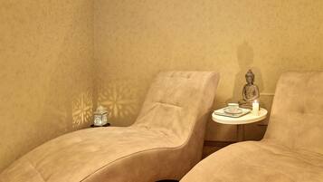 Um quarto com duas poltronas acolchoadas, uma mesa pequena com uma estátua e uma vela, e um candeeiro decorativo.