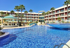 Um hotel com uma piscina grande, palmeiras e uma área de estar coberta.