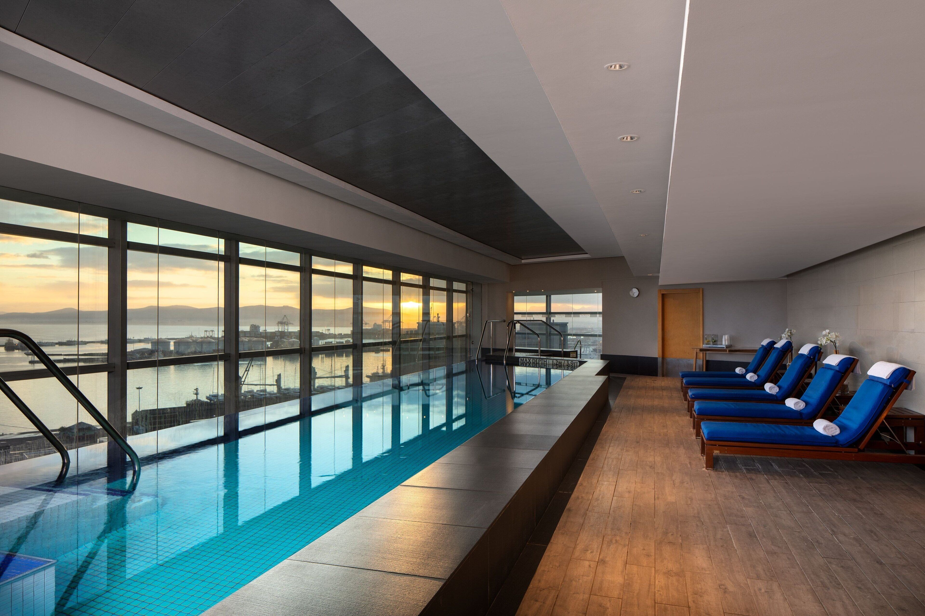 Piscina interna moderna com vista para a cidade, piso de madeira e espreguiçadeiras.