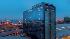 Um hotel Westin moderno com fachada de vidro, situado perto de uma orla com infraestrutura visível.