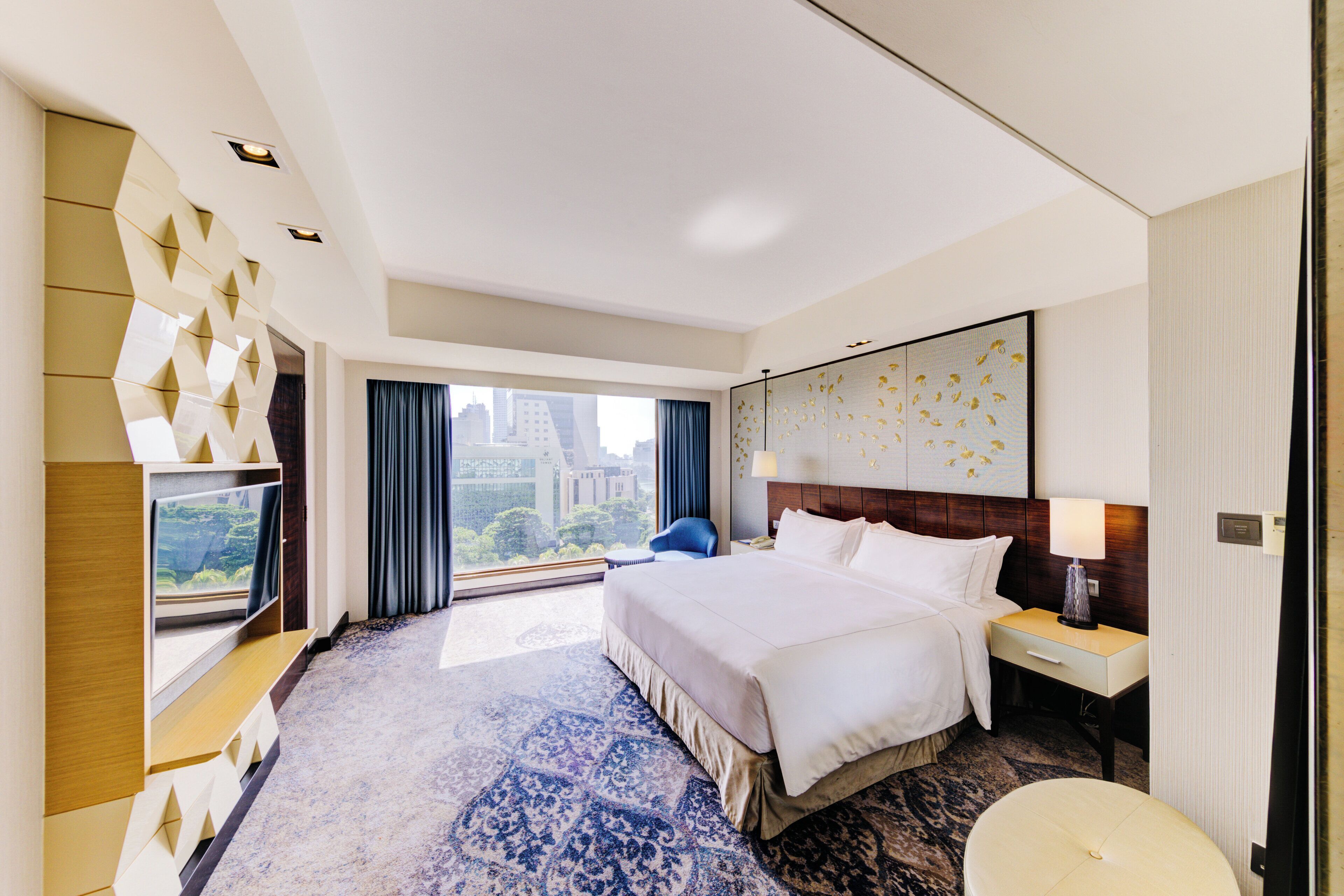 Quarto de hotel com uma cama grande, escrivaninha, cadeira, TV e vista para a cidade.