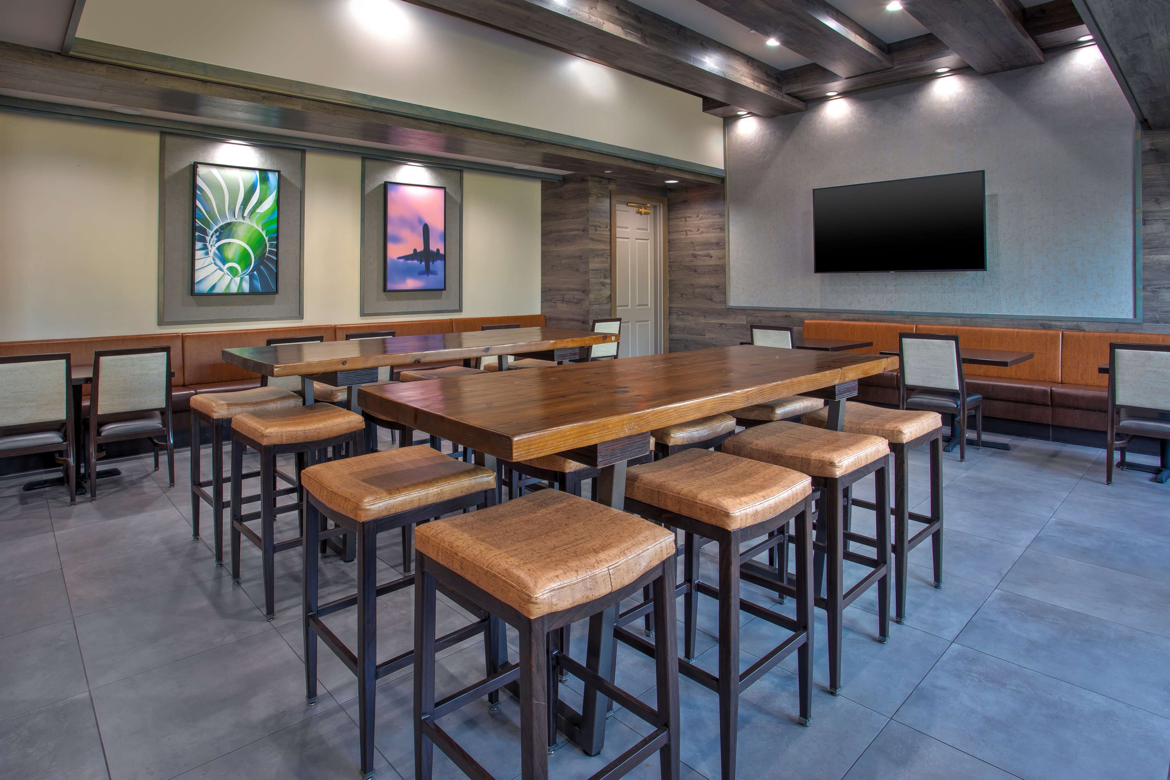 Uma sala de conferências com uma grande mesa de madeira rodeada por banquetas altas, uma TV de tela plana na parede e duas obras de arte emolduradas na parede.