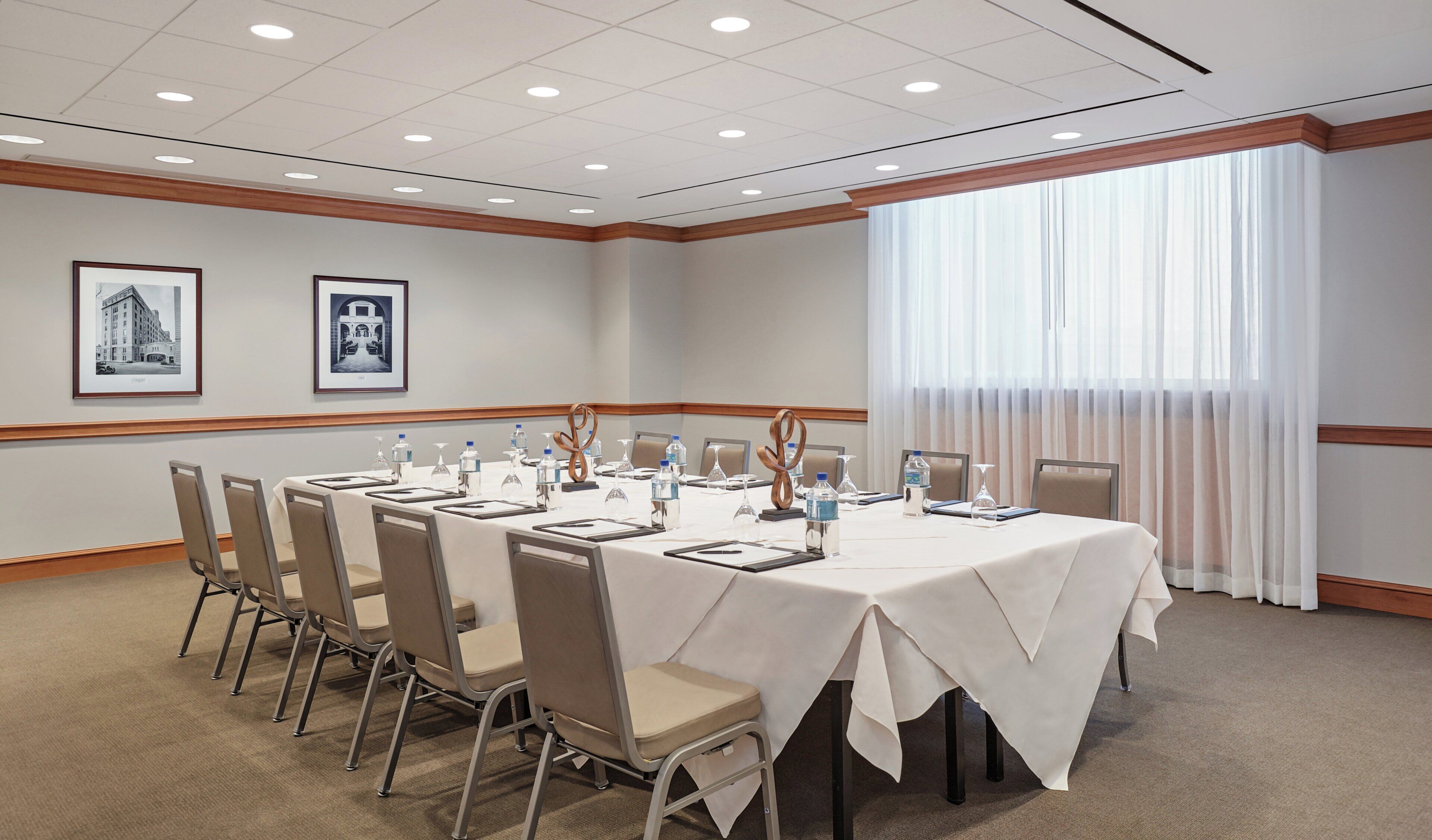 Sala de conferência com uma mesa comprida, cadeiras, garrafas de água, copos e quadros nas paredes.