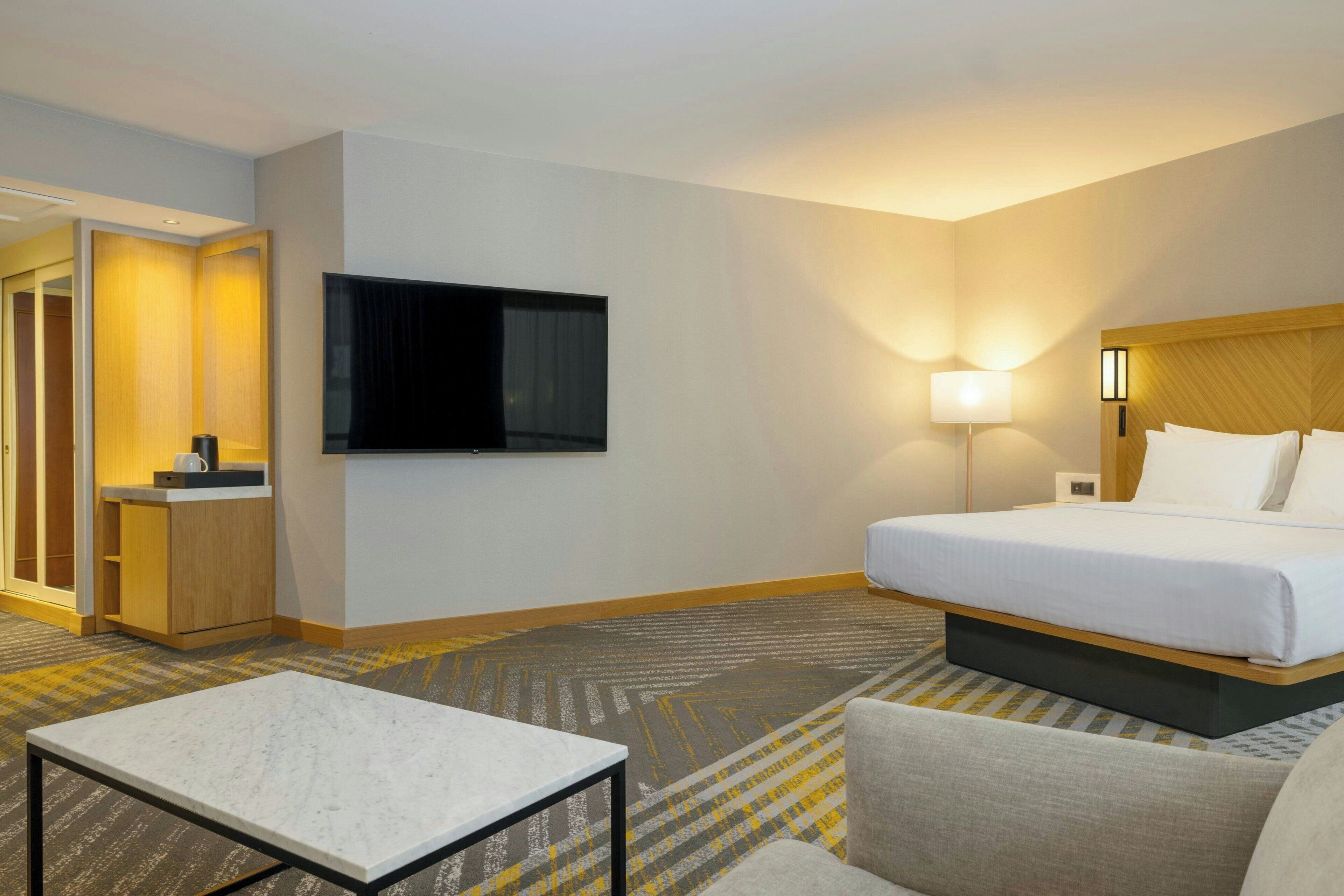 Quarto de hotel com uma cama, televisão, escrivaninha e sofá.