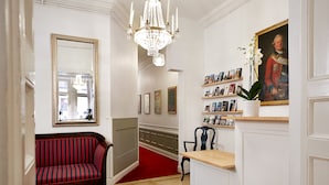 Um corredor com um sofá listrado em vermelho e preto, um candelabro, um retrato emoldurado e uma estante de livros com livros e objetos decorativos.