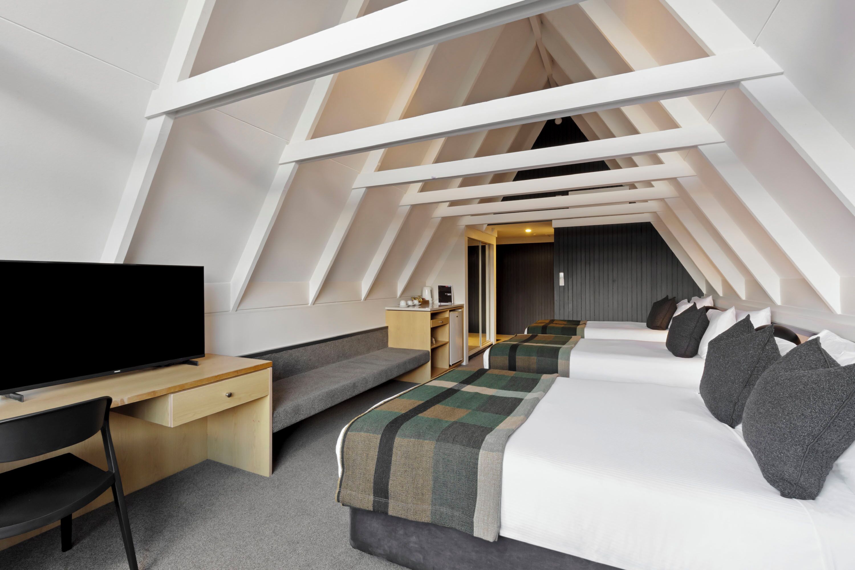 Quarto moderno em formato triangular, com cama, escrivaninha e televisão.