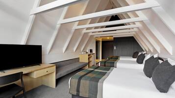 Quarto moderno em formato triangular, com cama, escrivaninha e televisão.
