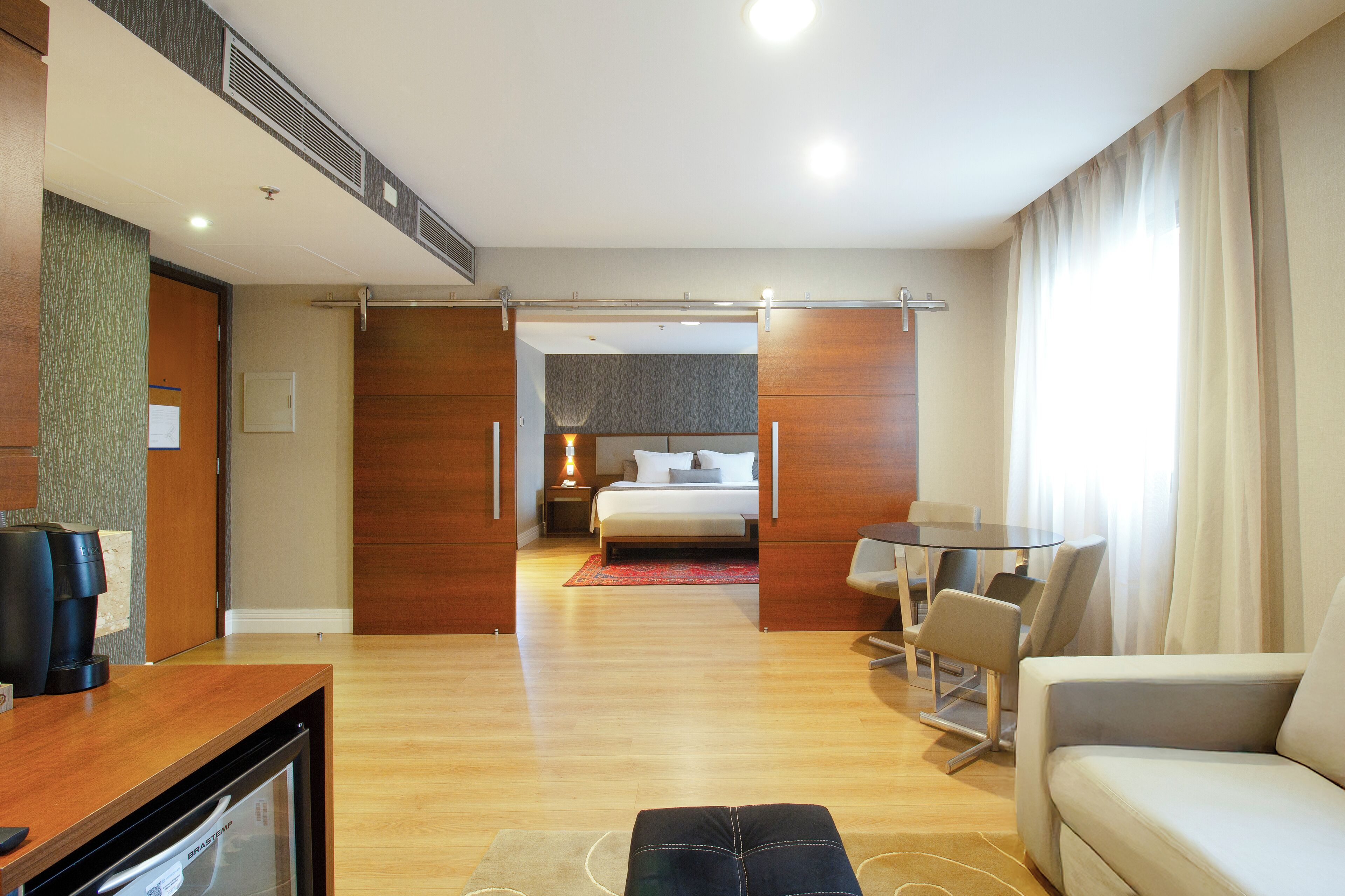Quarto de hotel com cama, escrivaninha, cadeira, sofá e mesa de jantar.