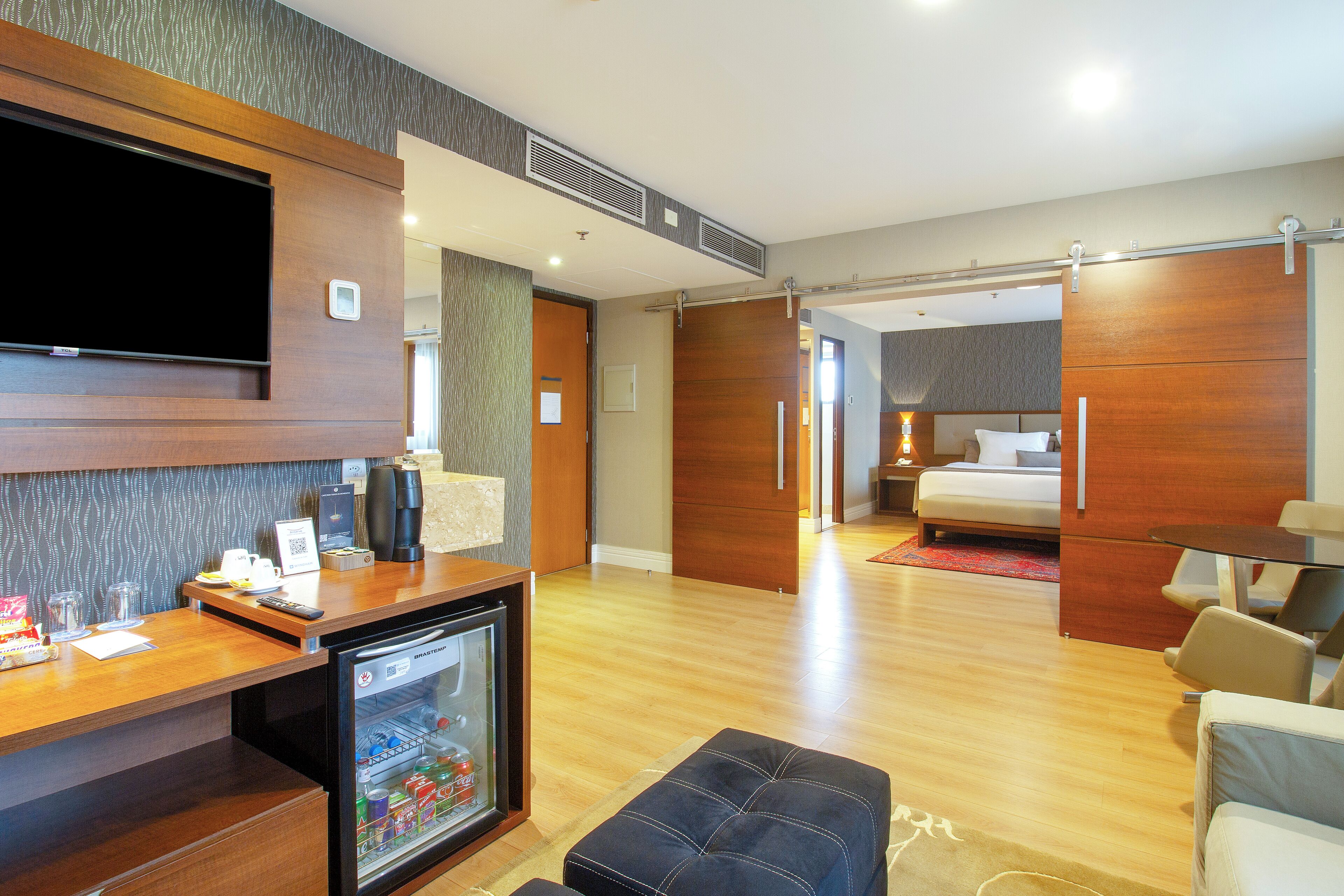 Quarto de hotel com televisão, minibar, área de estar e uma cama.