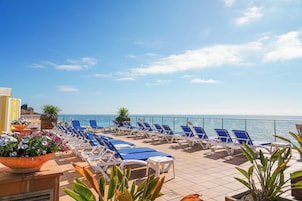 Terraço no telhado com espreguiçadeiras, plantas em vasos e vista para o mar.