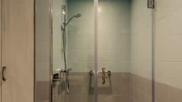 Um banheiro moderno com chuveiro em box de vidro, banheira branca e piso revestido de azulejos.