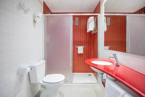 Um banheiro com vaso sanitário branco, pia vermelha e chuveiro com box de vidro.