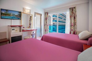 Quarto de hotel com duas camas, uma escrivaninha, um mini-frigobar e uma janela com vista para uma varanda.