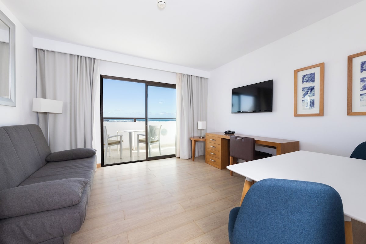 Quarto de hotel moderno com varanda, sofá, escrivaninha e televisão.