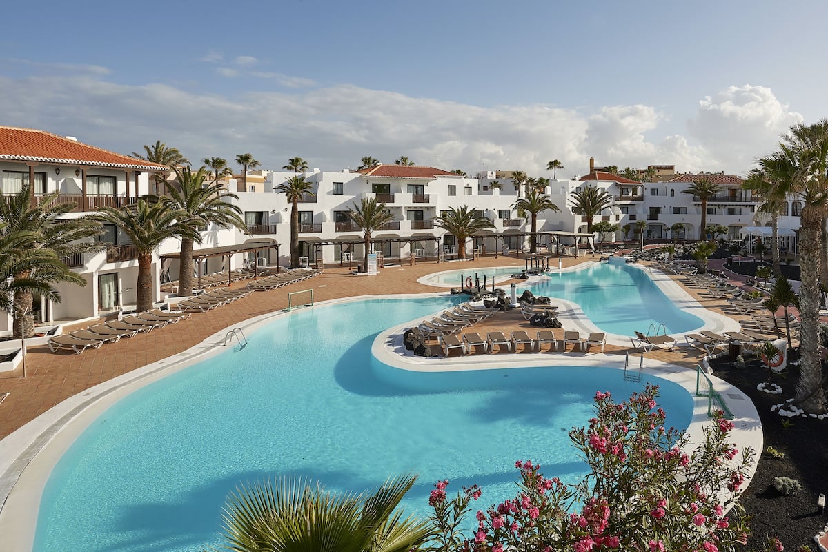 Um resort com uma piscina grande, espreguiçadeiras e palmeiras.