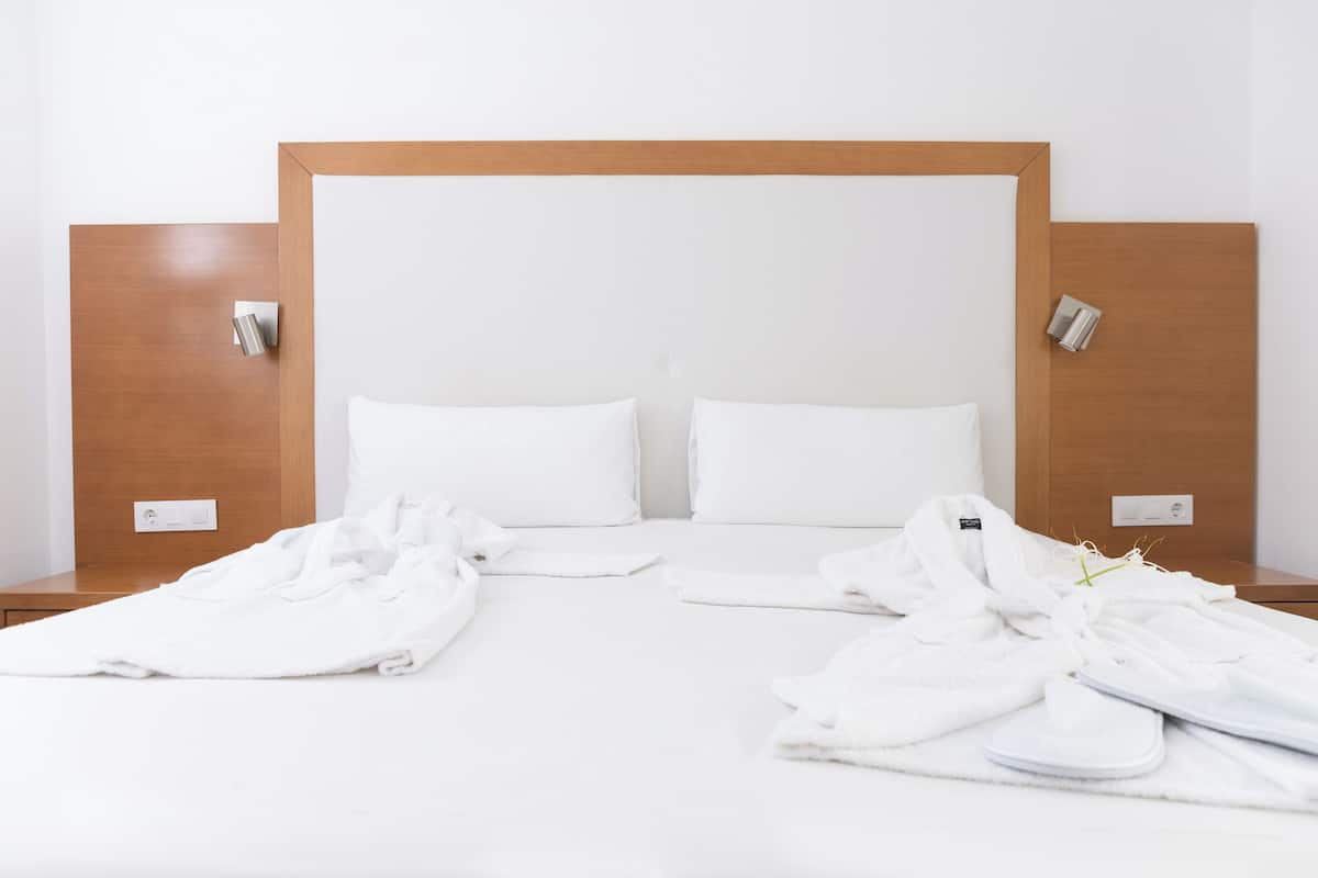 Cama bem arrumada com lençóis brancos e cabeceira de madeira.