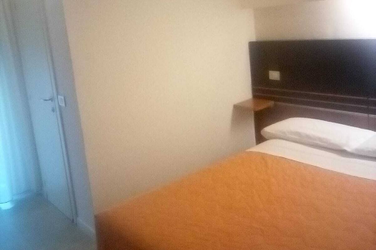 Quarto de hotel com cama, mesa de cabeceira e porta.