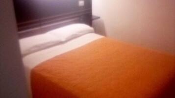 Uma cama de solteiro com colcha laranja num quarto com parede branca e cabeceira de madeira.