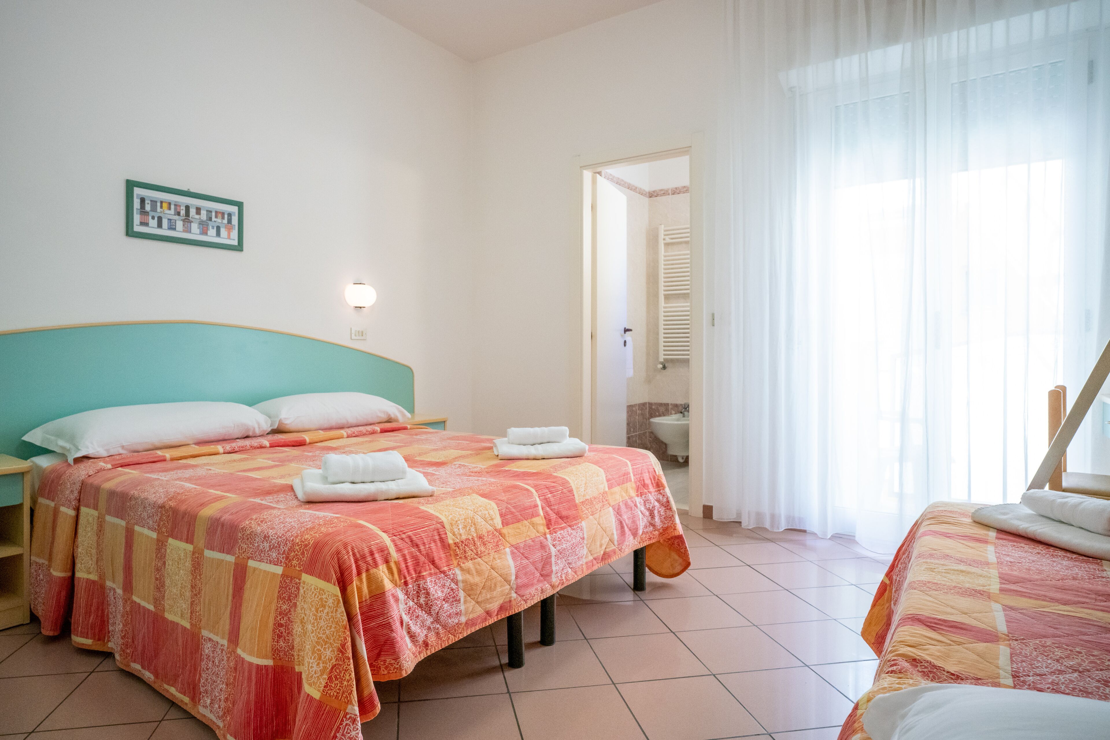 Quarto de hotel com duas camas, banheiro e vista para o mar.